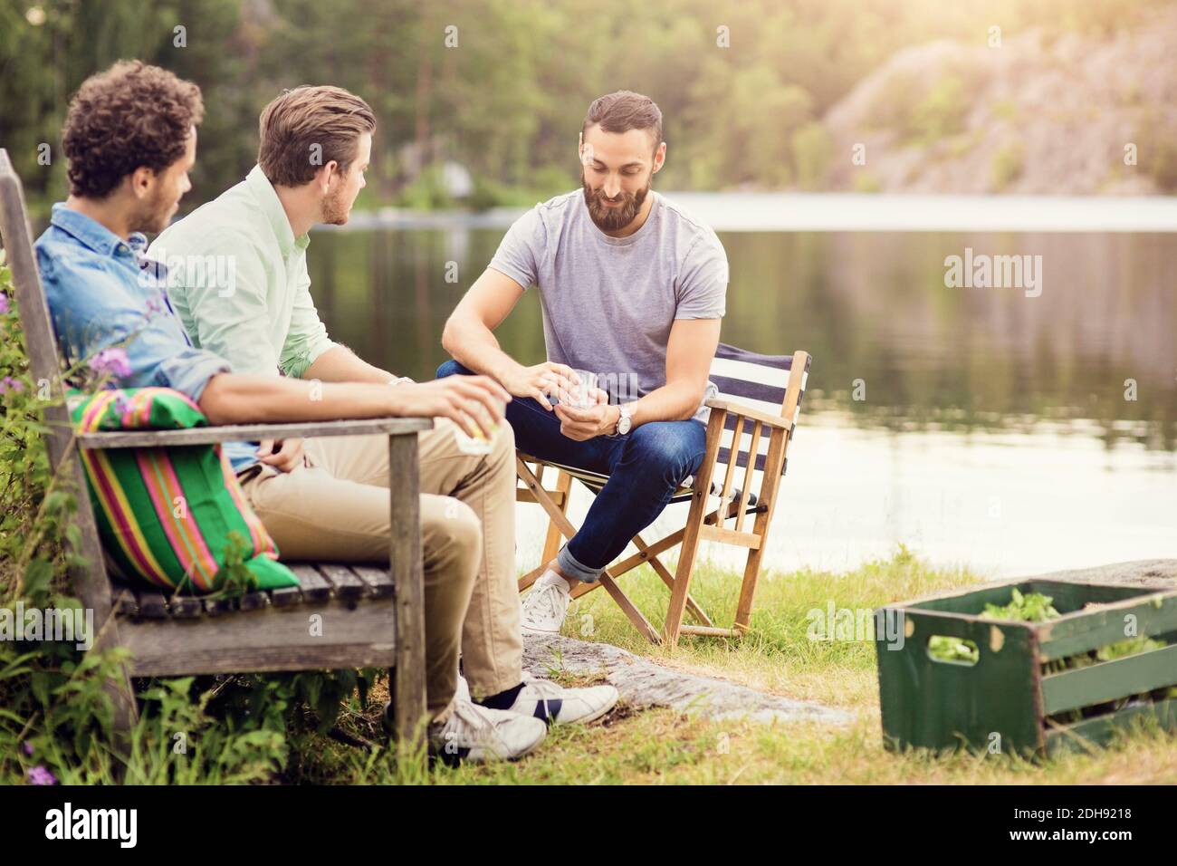 Friends having drink while sitting on bench at lakeshore Stock Photo ...
