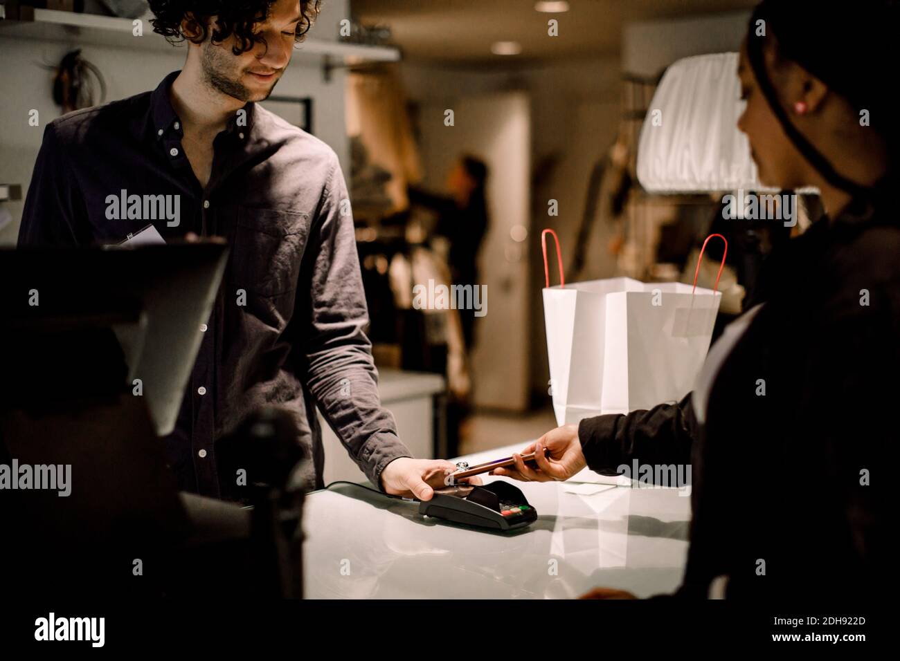 Side view of female customer paying through smart phone at store Stock ...