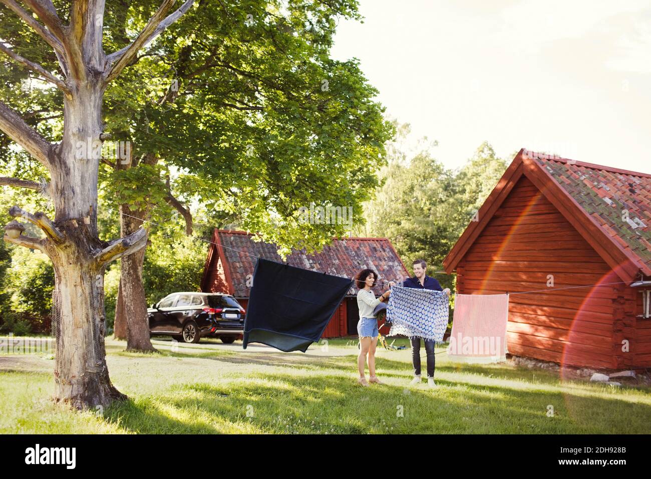 Full length of man and woman drying clothes in backyard on sunny day ...