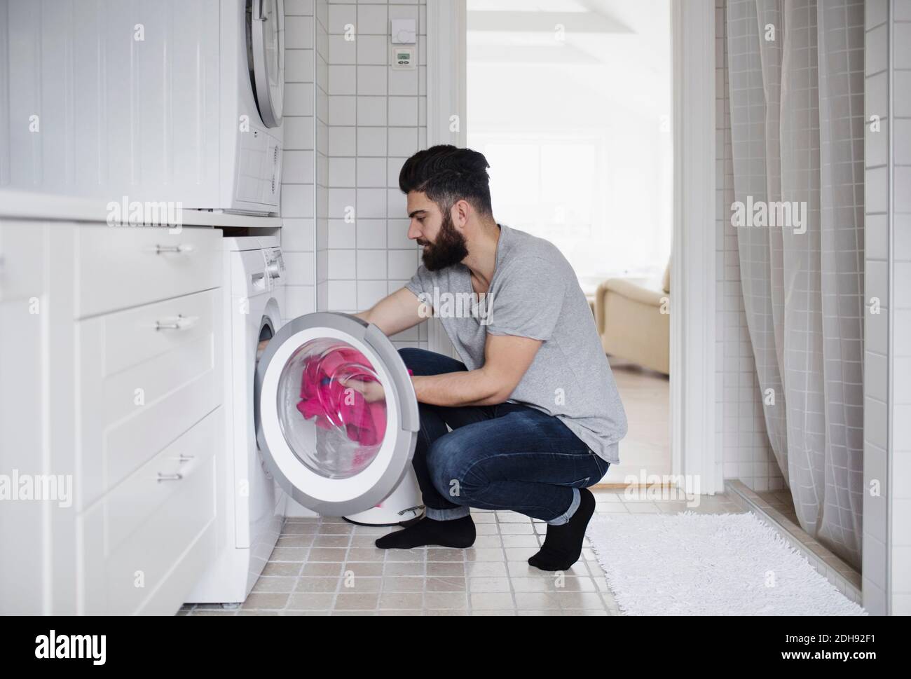 Side view of man crouching while loading clothes in washing machine at ...