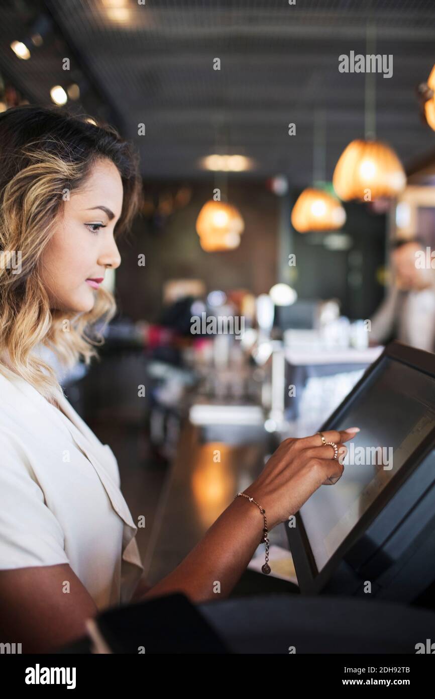 Side view of female owner touching cash register at checkout in ...