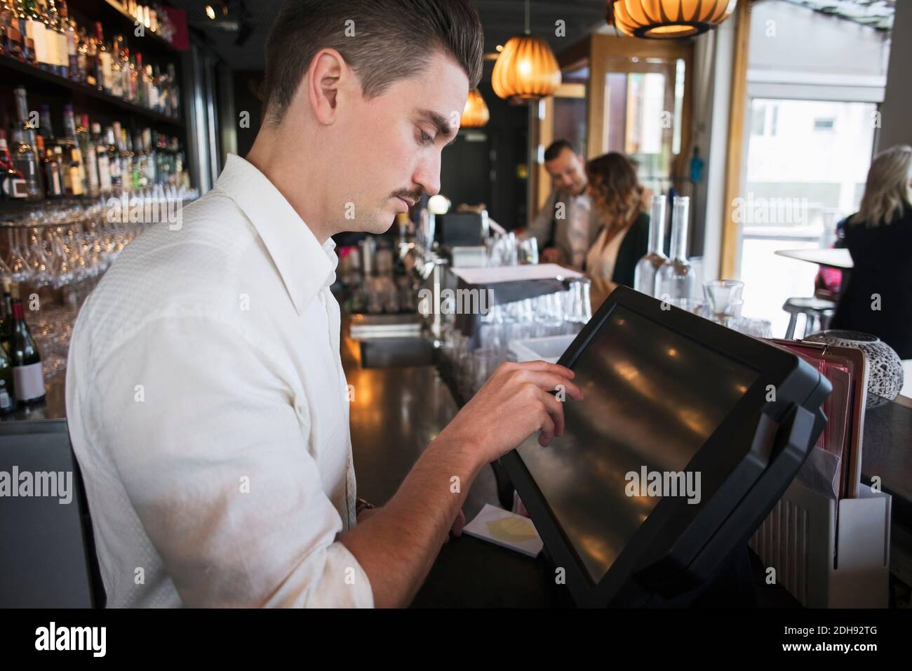 Side view of male owner using cash register at checkout in restaurant ...