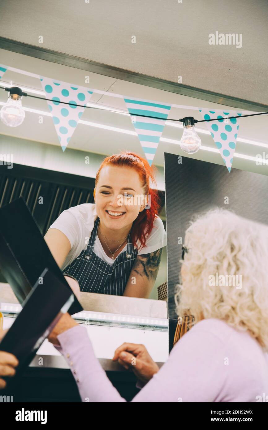 Smiling owner explaining menu to senior customer while standing in food ...