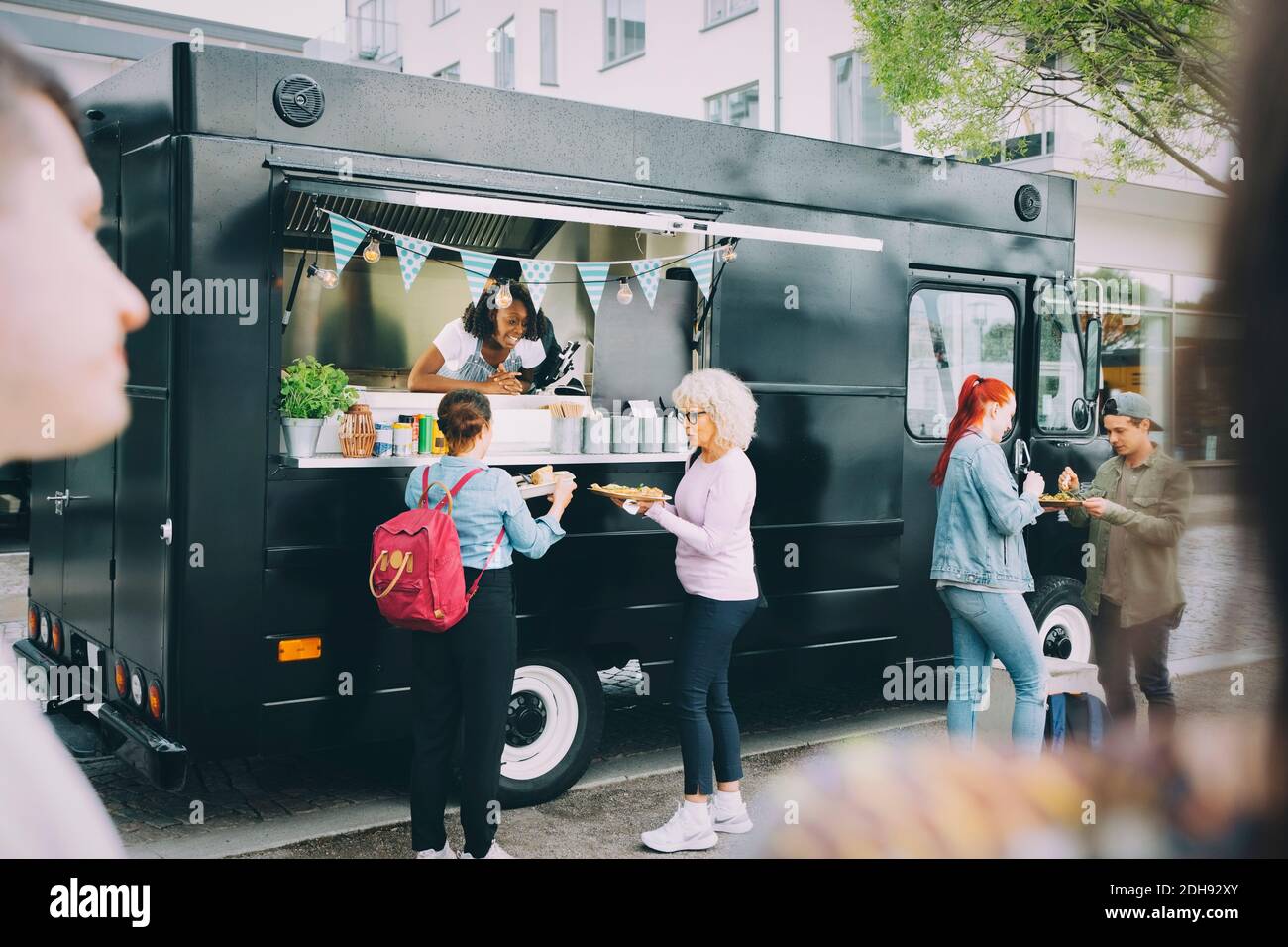Female owner giving street food to customers while standing in ...