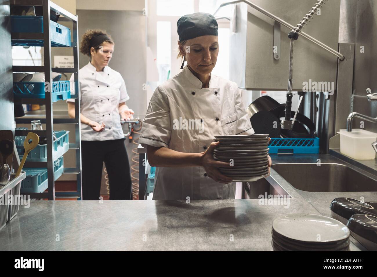 Female chef holding plates while coworker standing in background in ...