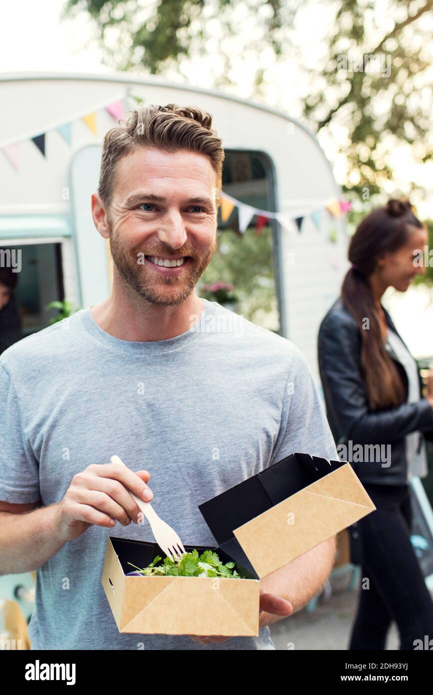 Happy male customer holding disposable salad box against food truck ...