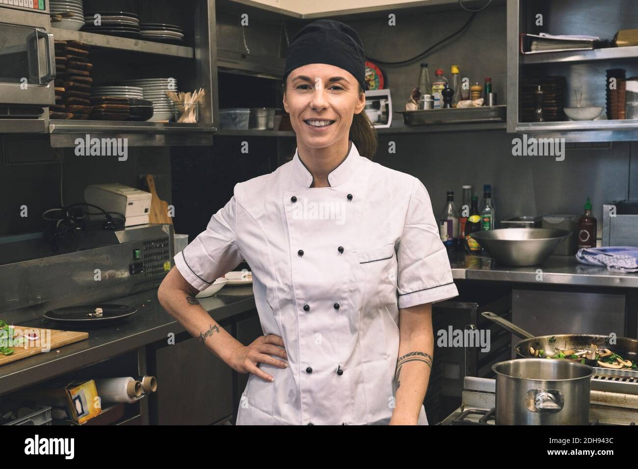 Portrait of smiling female chef with hand on hip in commercial kitchen ...