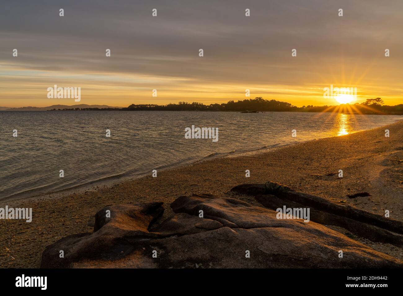 beautiful sunset on sand and rock beach with gentle waves under an ...