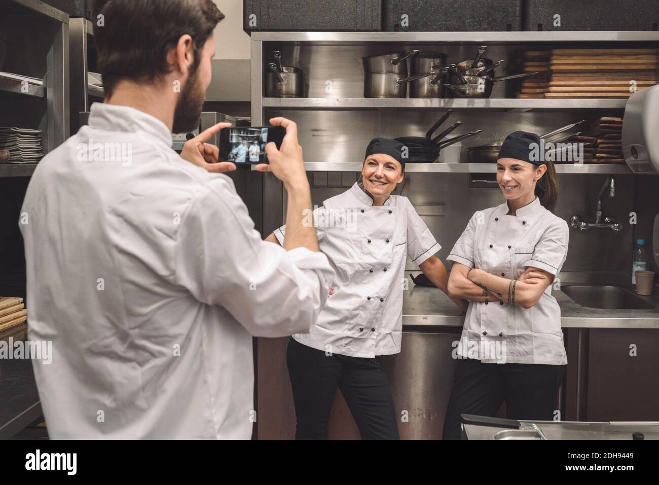 Male chef taking photograph of smiling female coworkers in commercial ...