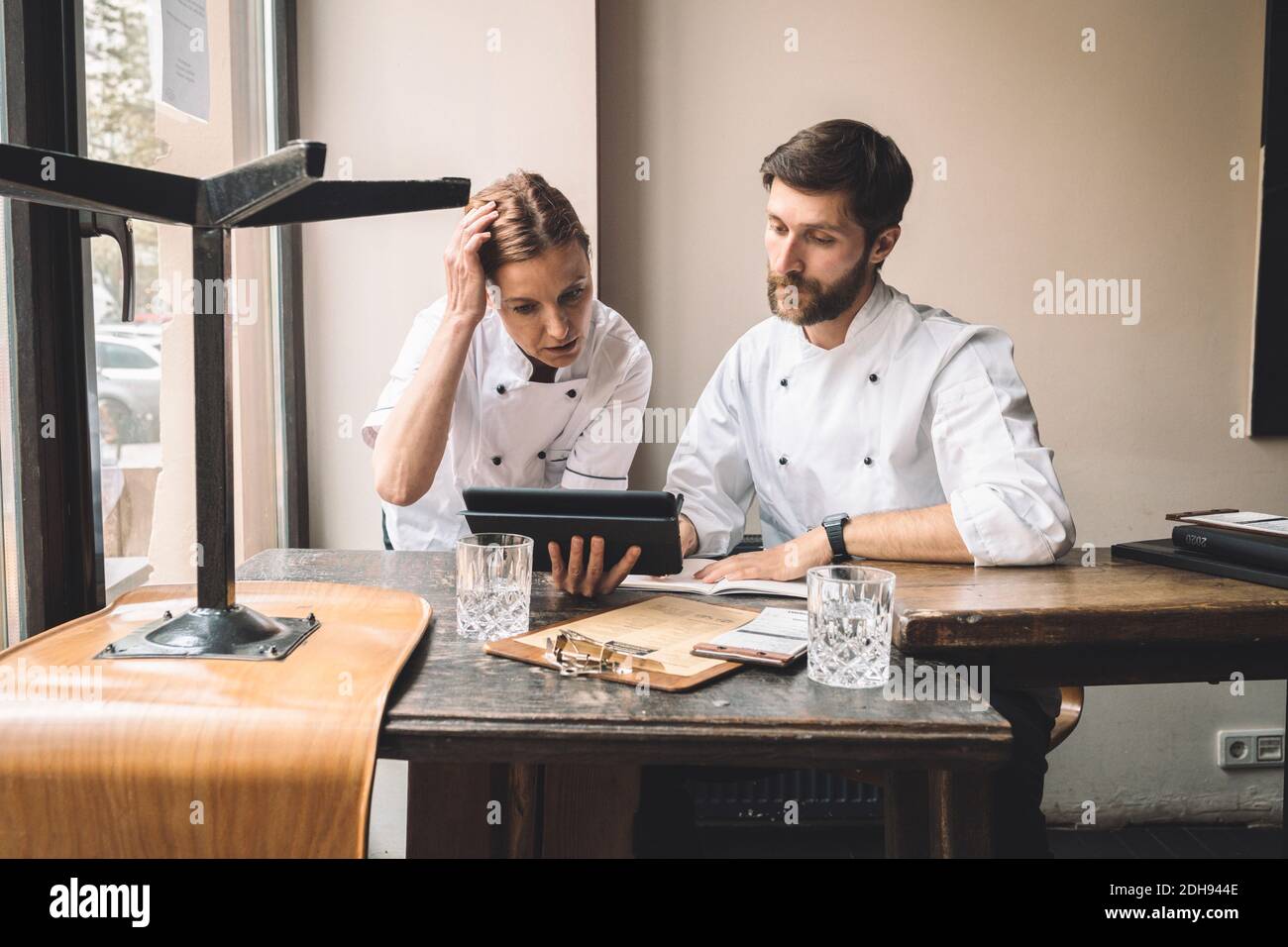 Chef with coworker looking at digital tablet at table in restaurant ...
