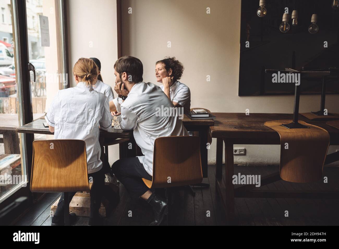 Male chef discussing with female coworkers at table in restaurant Stock ...
