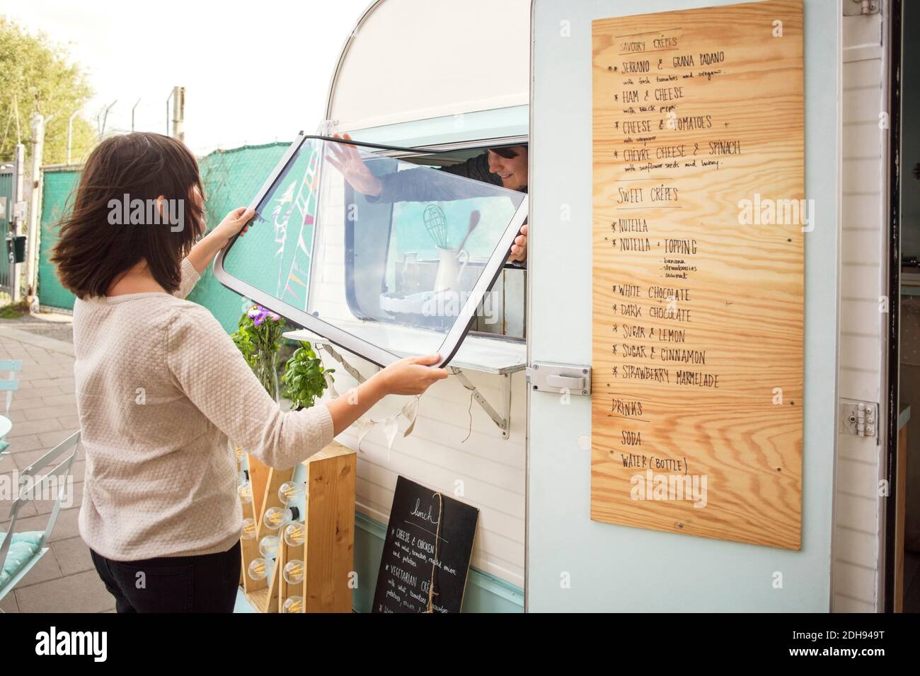 Rear view of female owner opening window at food truck with male ...