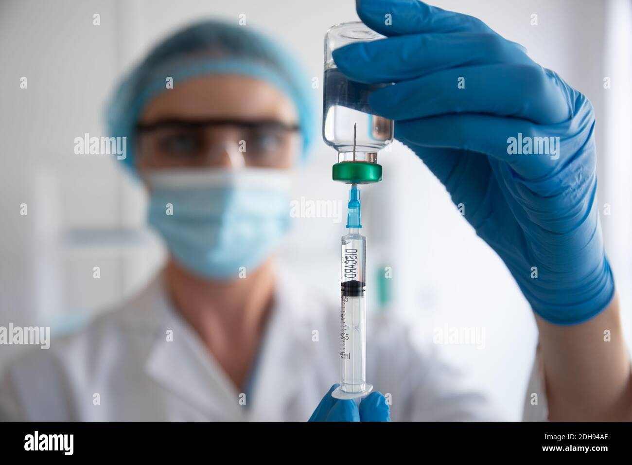 Female doctor wearing face mask injecting syringe into a vial bottle ...