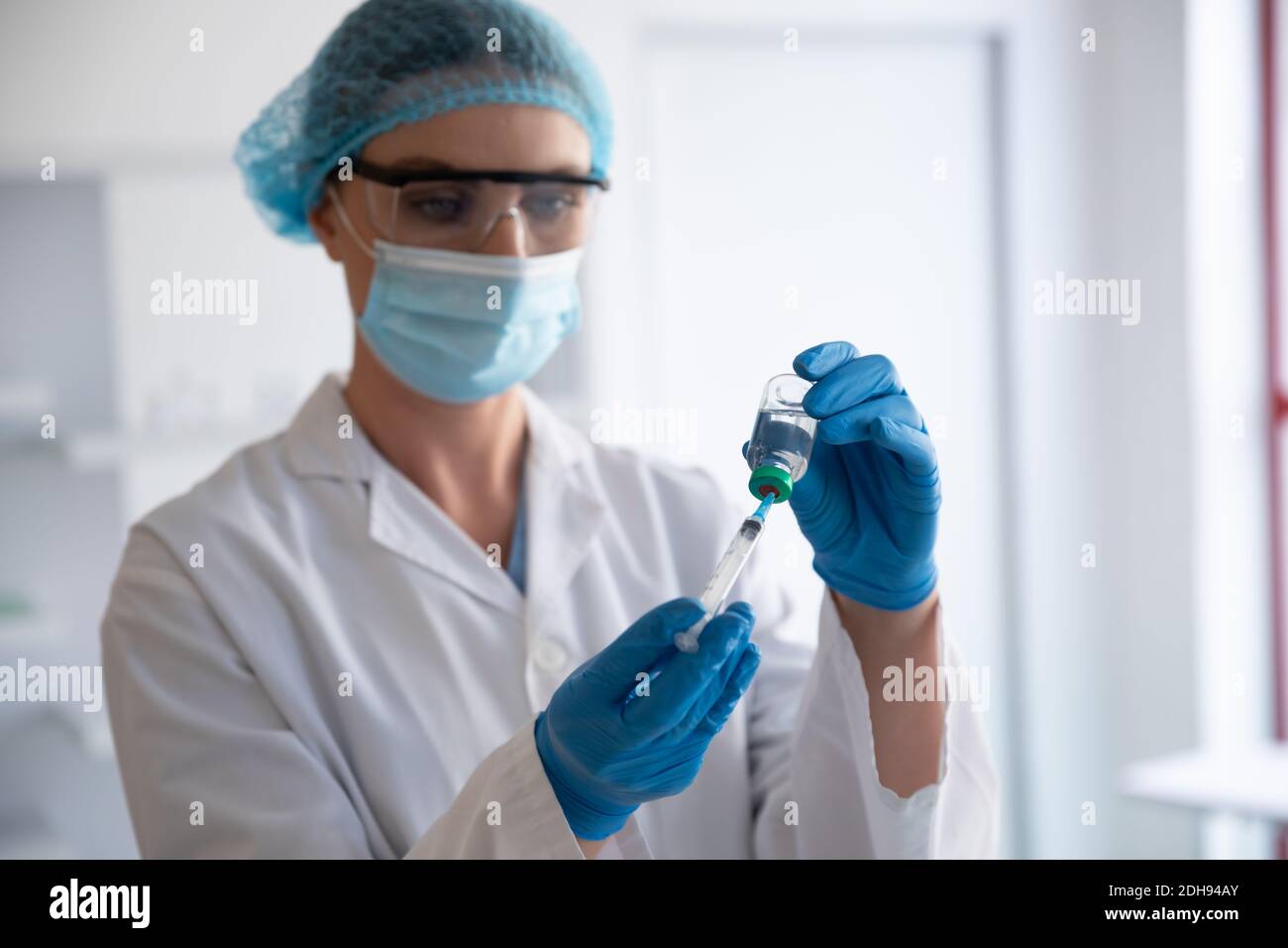 Female doctor wearing face mask injecting syringe into a vial bottle ...
