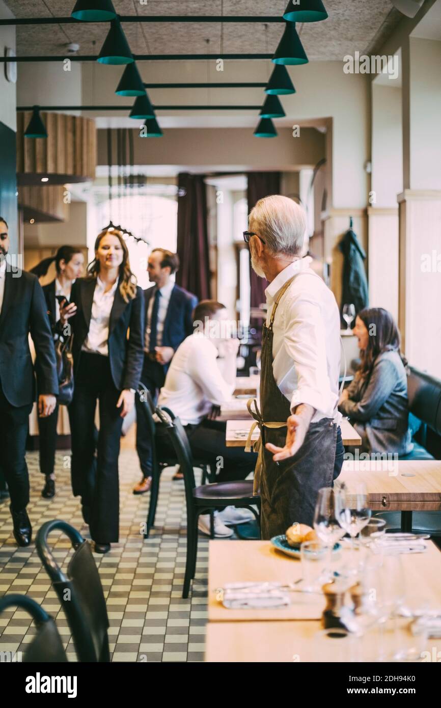 Side view of waiter showing table to business people in restaurant ...