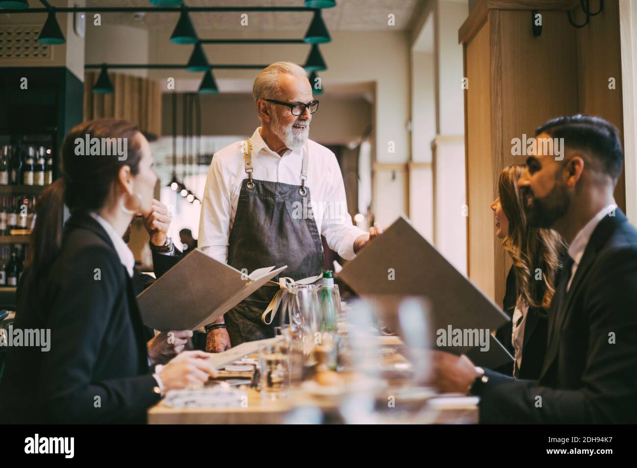 Waiter talking to business people while standing by table in restaurant ...