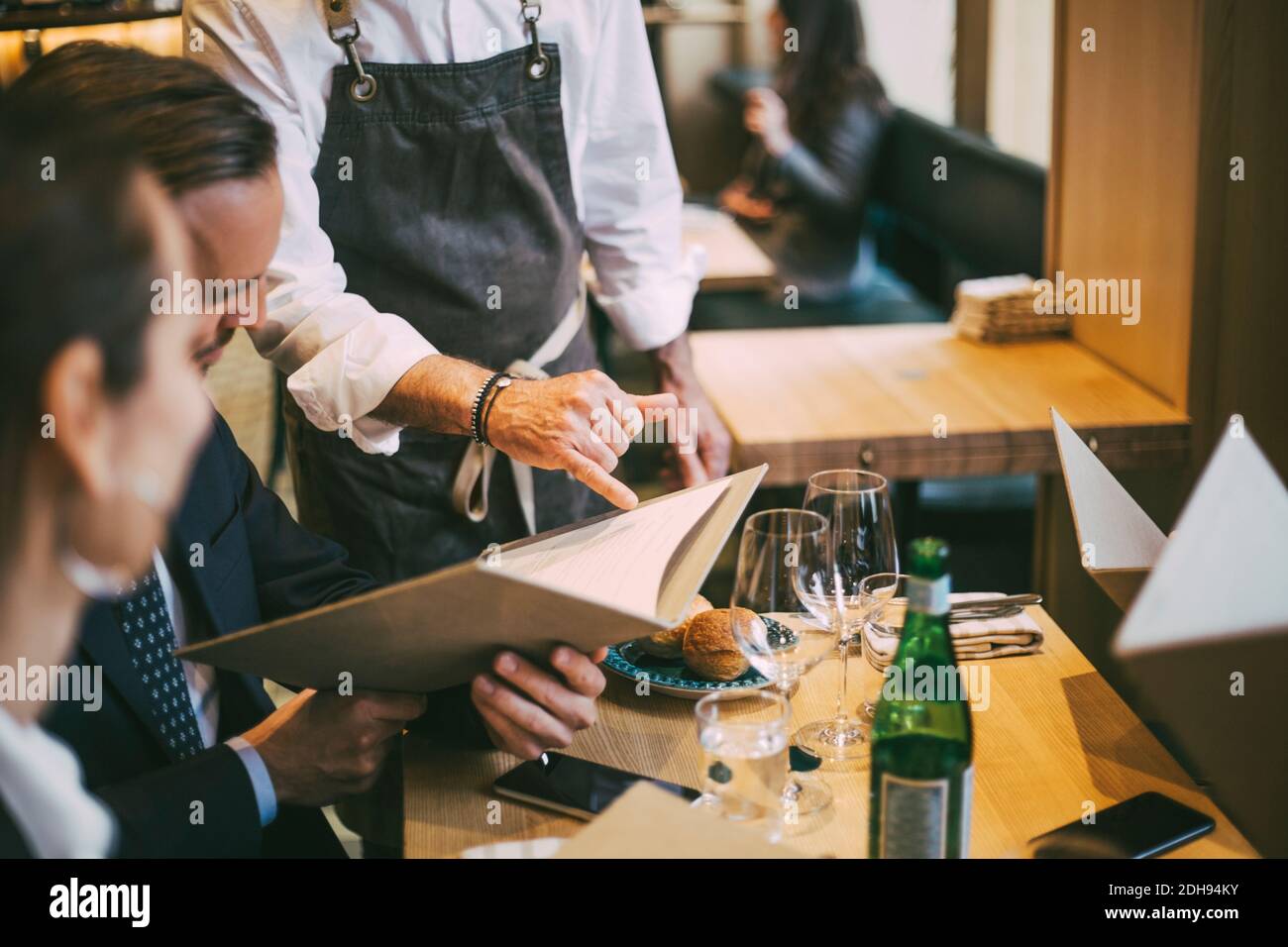 Midsection of waiter pointing at menu while business professionals ...