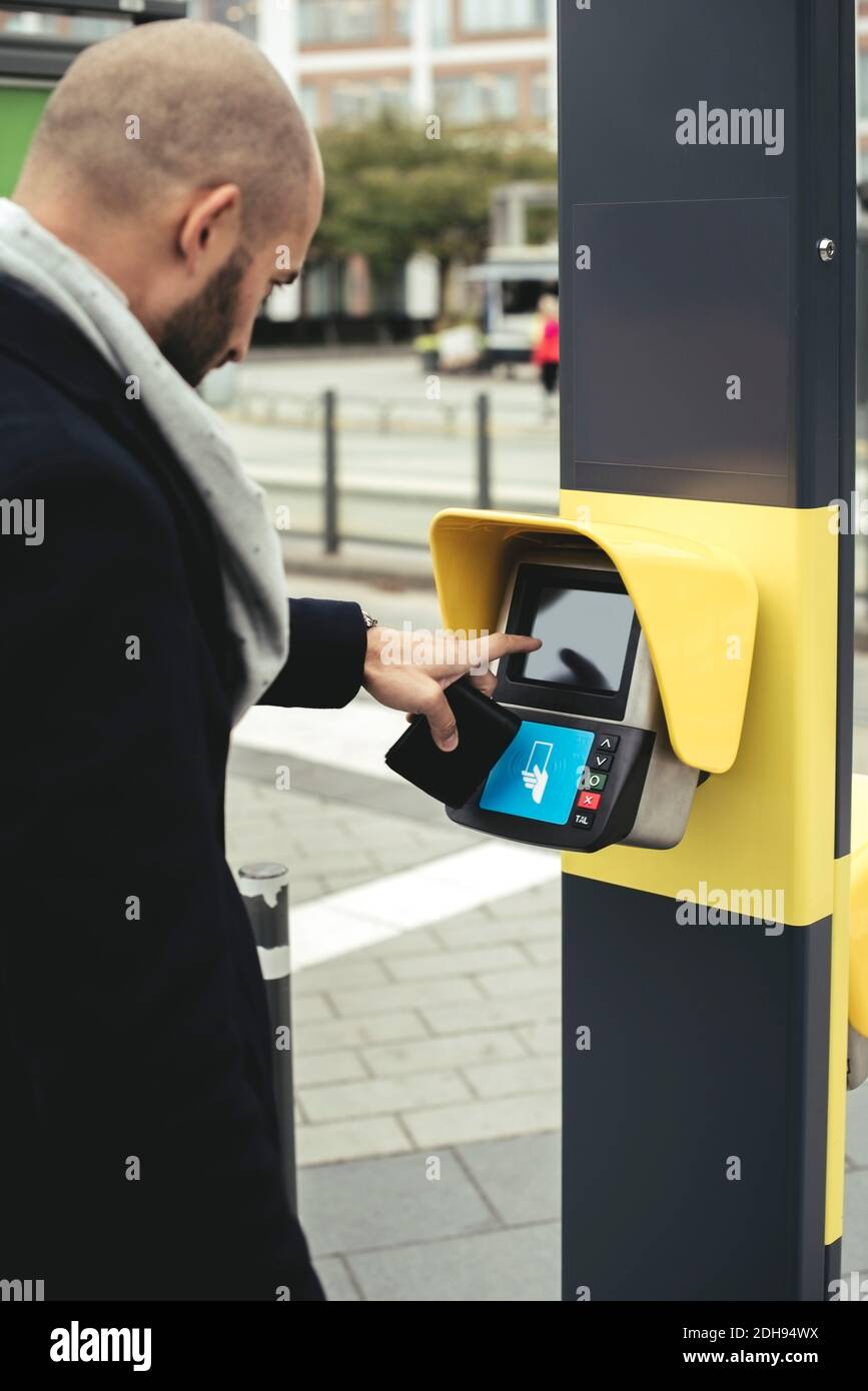 Side view of businessman operating ticket scanner on sidewalk in city ...