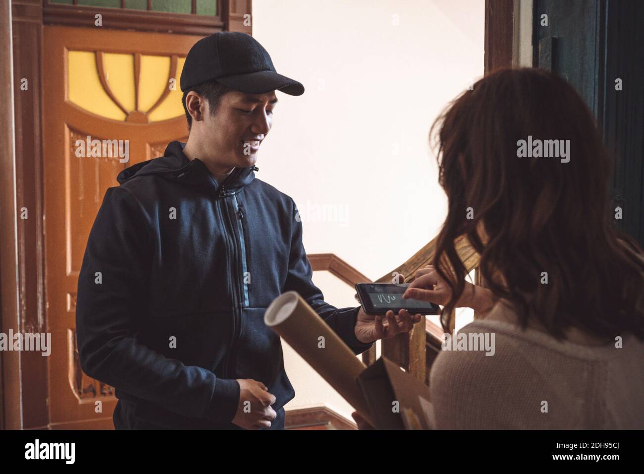 Customer signing on smart phone while delivery man standing at doorstep ...