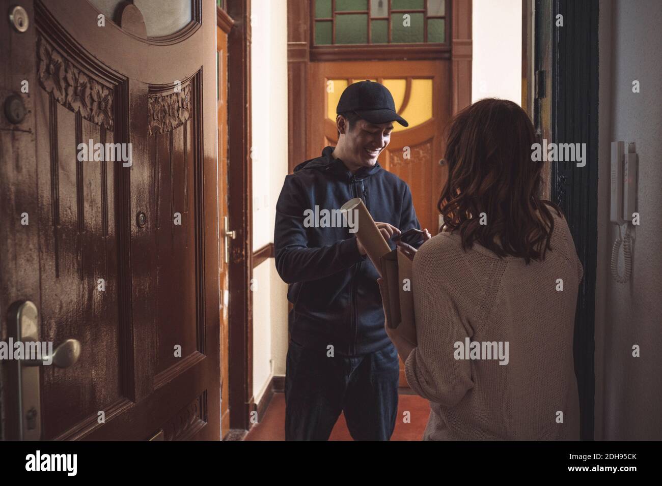 Rear view of customer holding package while delivery man using phone at ...