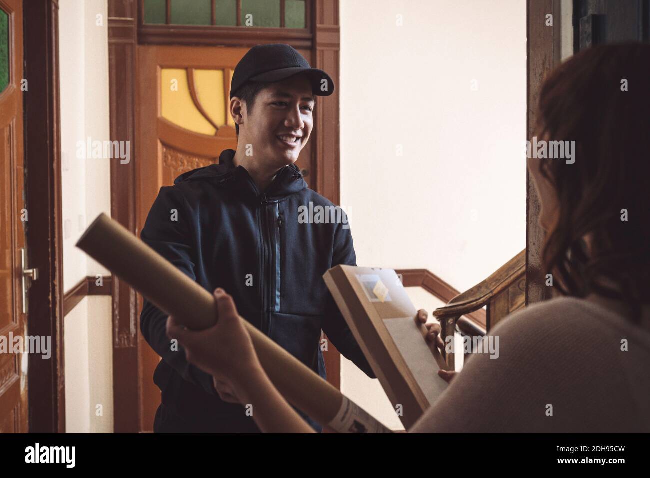 Smiling delivery man delivering package while talking to customer at ...