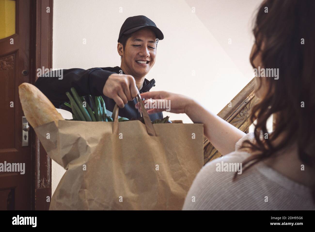 Smiling delivery man delivering vegetables to customer while talking at ...