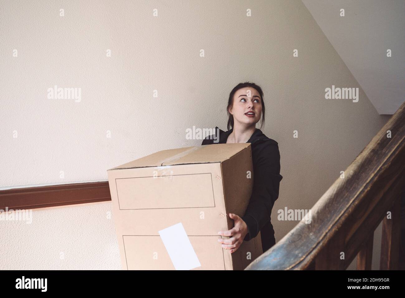 Delivery woman with cardboard box looking up against wall Stock Photo ...