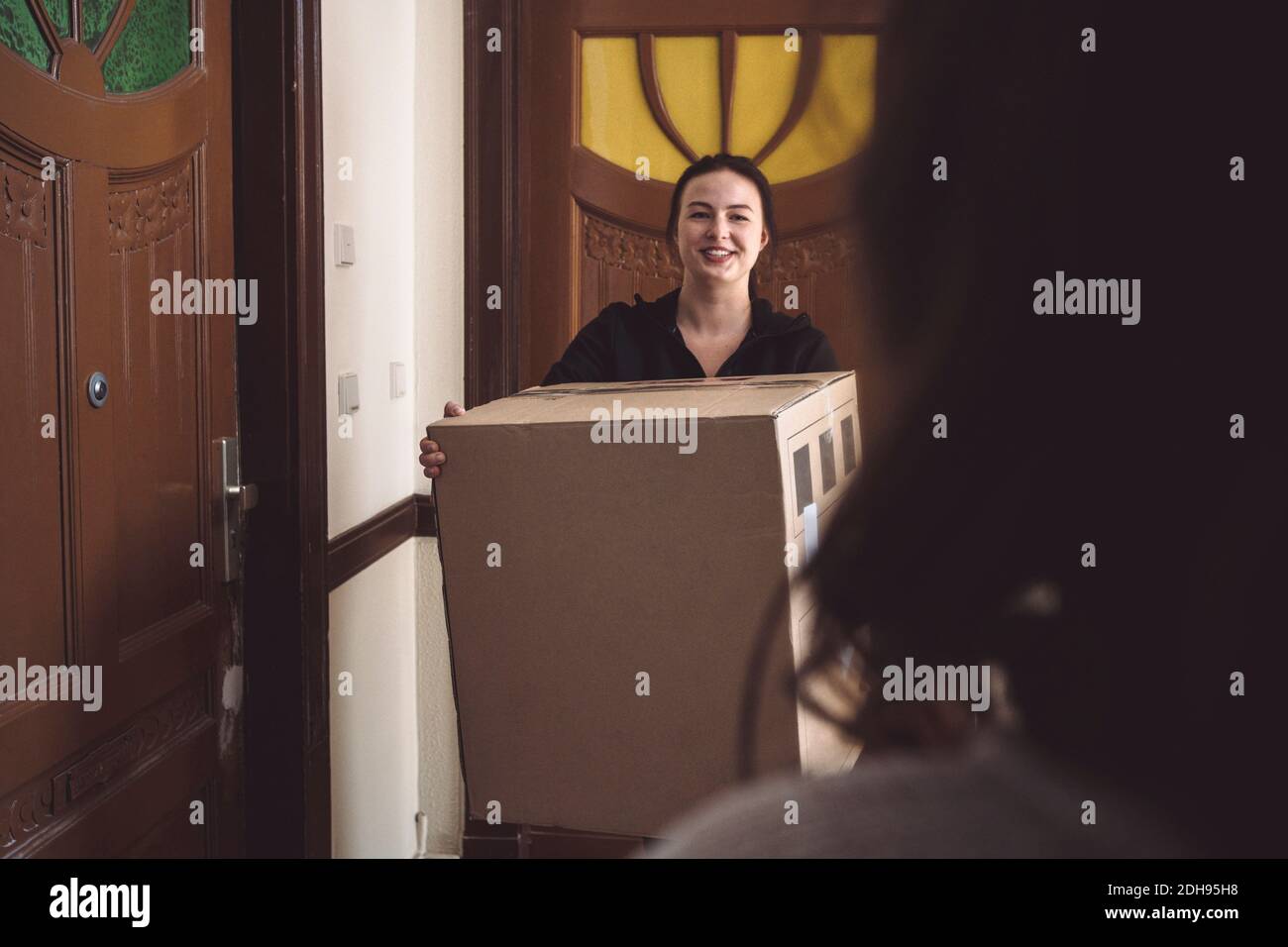 Smiling delivery woman delivering package to customer at doorstep Stock ...
