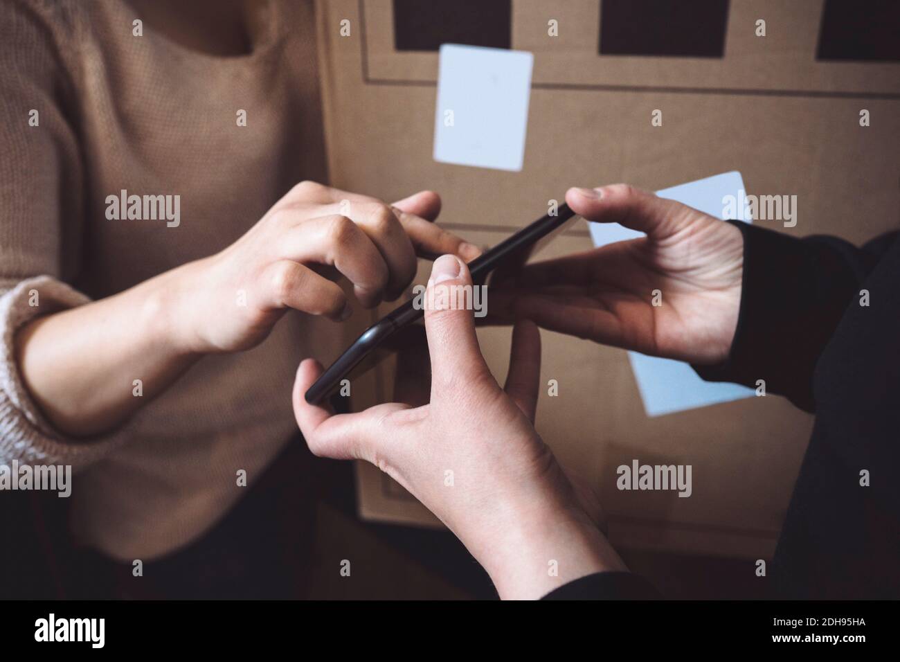 Midsection of customer signing on phone while holding package at ...