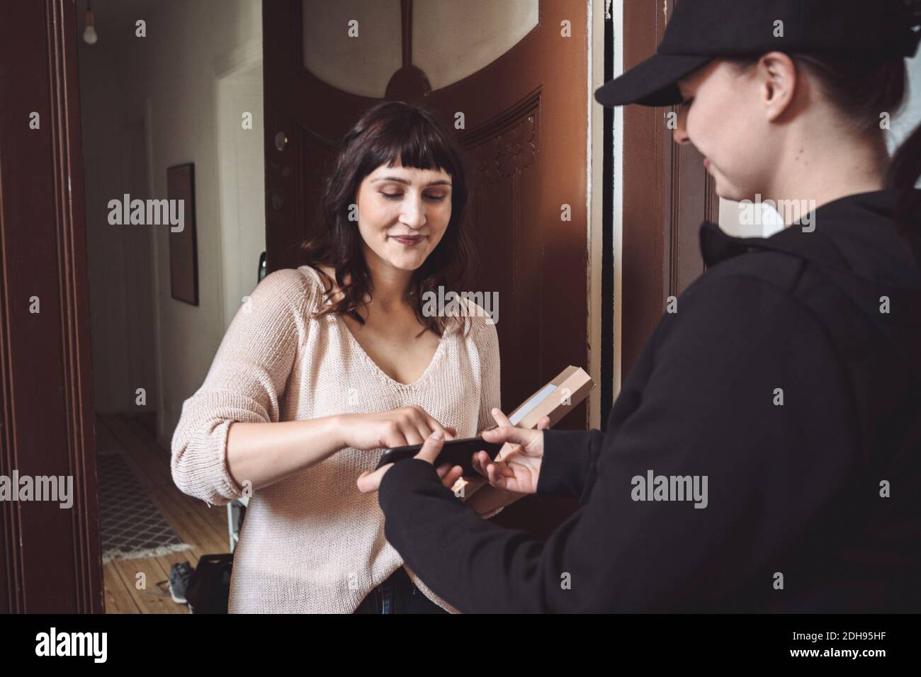 Smiling customer signing on smart phone while holding package at ...