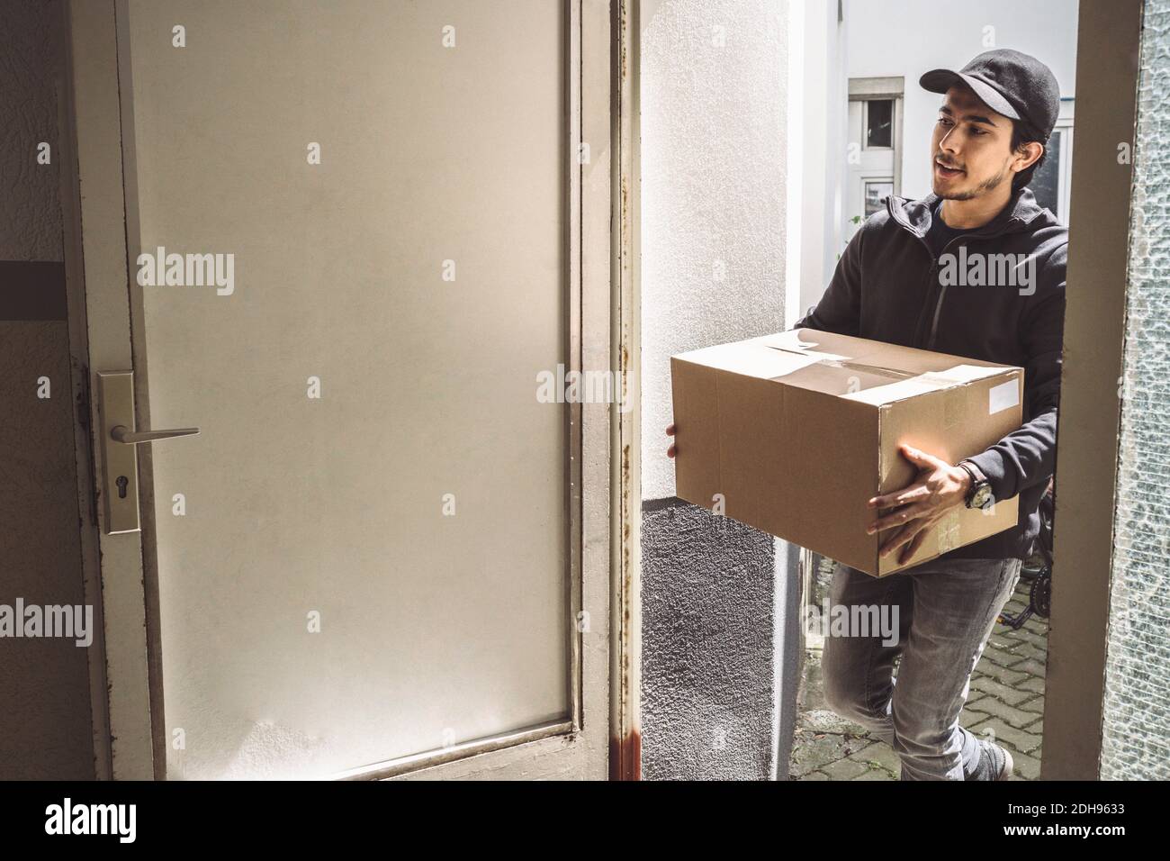 Confident delivery man with package standing at doorstep Stock Photo ...