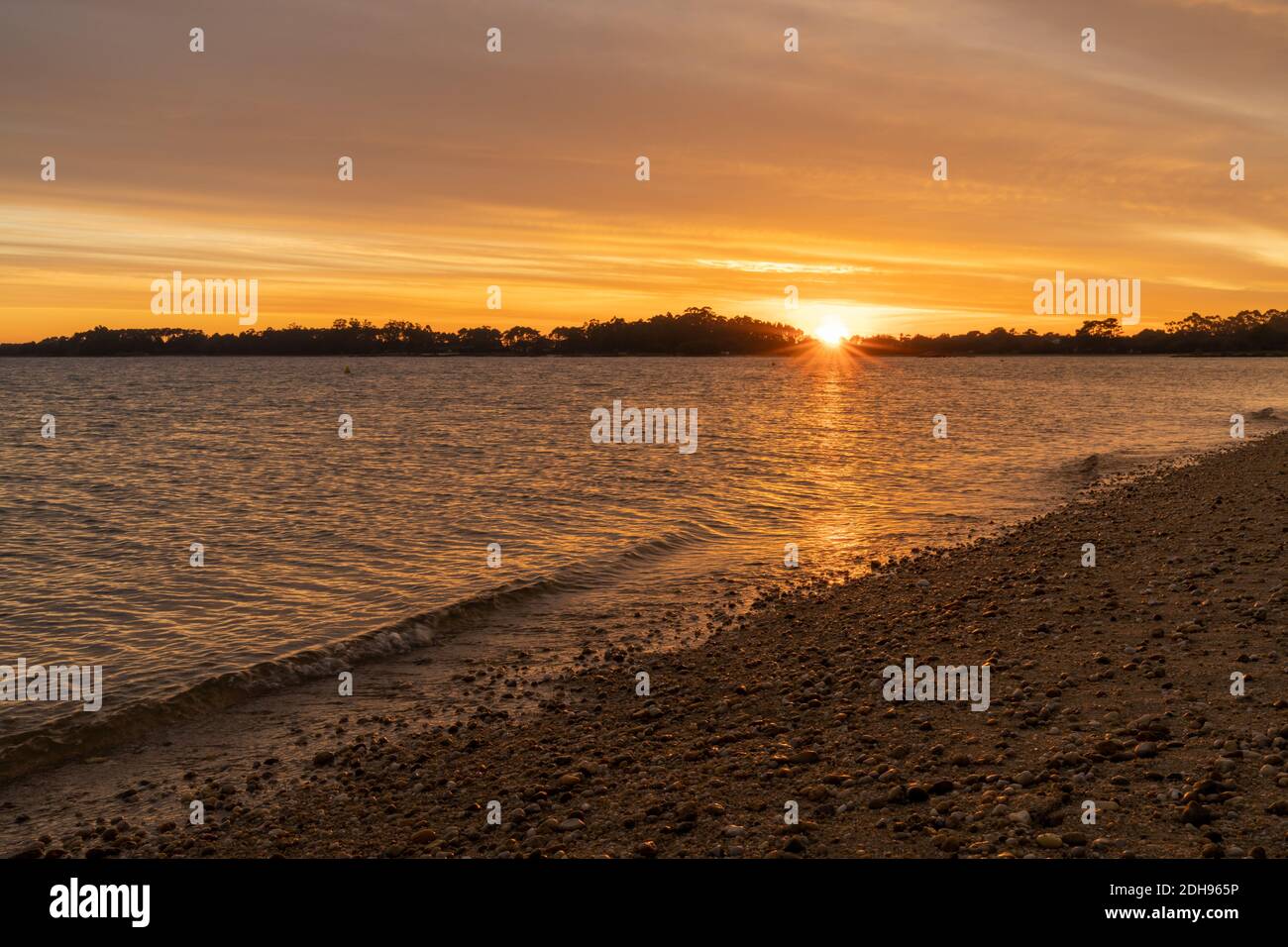 beautiful sunset on sand and rock beach with gentle waves under an ...