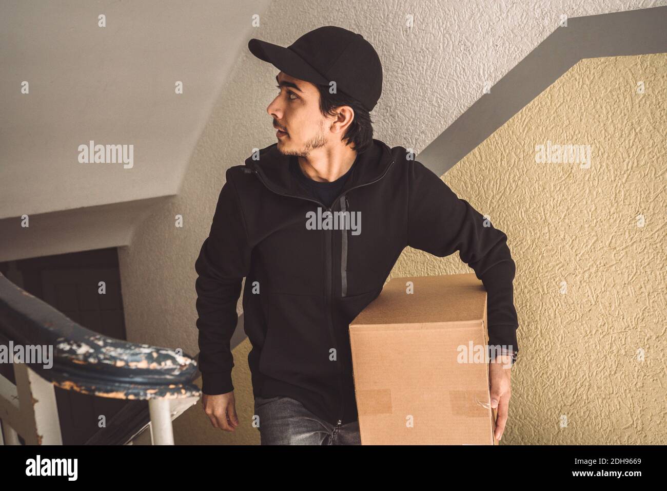 Delivery man with package looking away while walking on staircase Stock ...