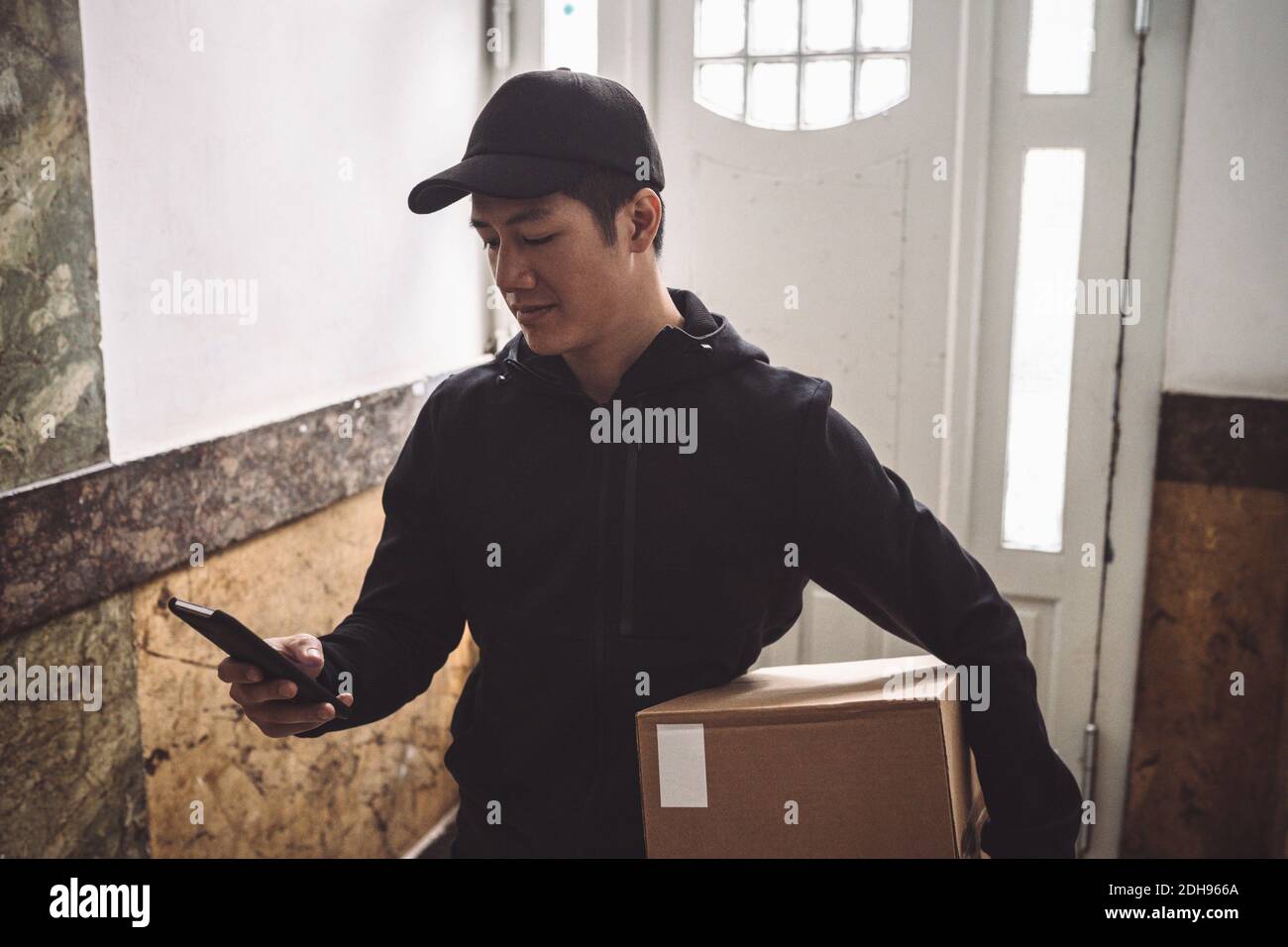 Delivery man using mobile phone while holding package against door ...