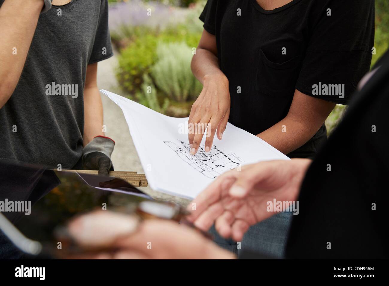 Midsection of female garden architect explaining blueprint to ... Midsection of female garden architect explaining blueprint to ...