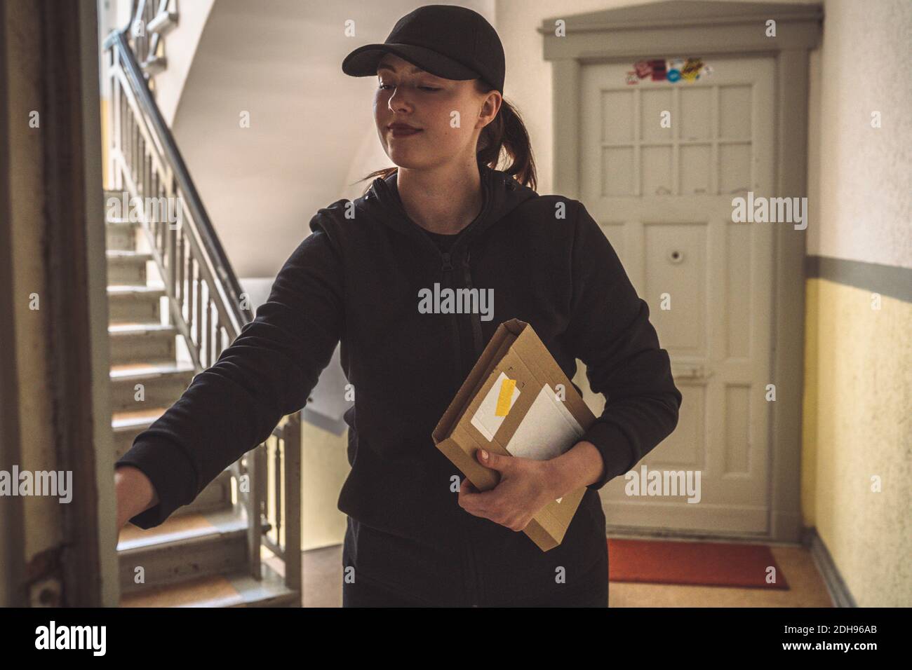 Confident delivery woman with package standing at doorstep Stock Photo ...