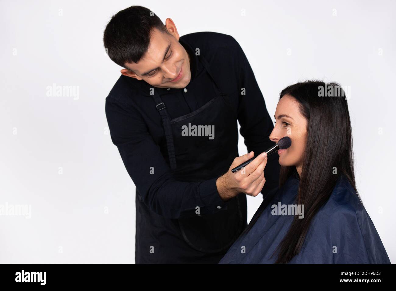 Cool male make-up artist doing makeup to young businesswoman. Beauty ...