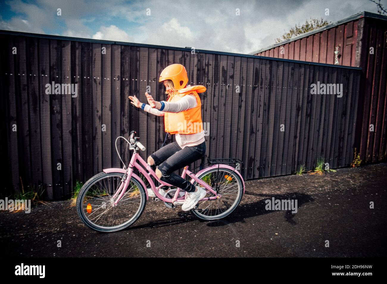 Smiling girl riding bicycle with arms outstretched on road Stock Photo ...