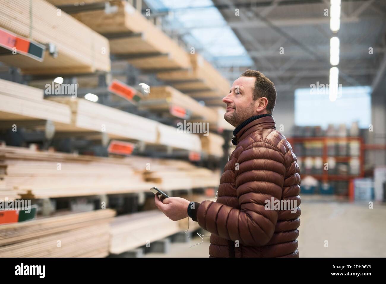 Customer looking at wooden planks on shelves while holding smart phone ...