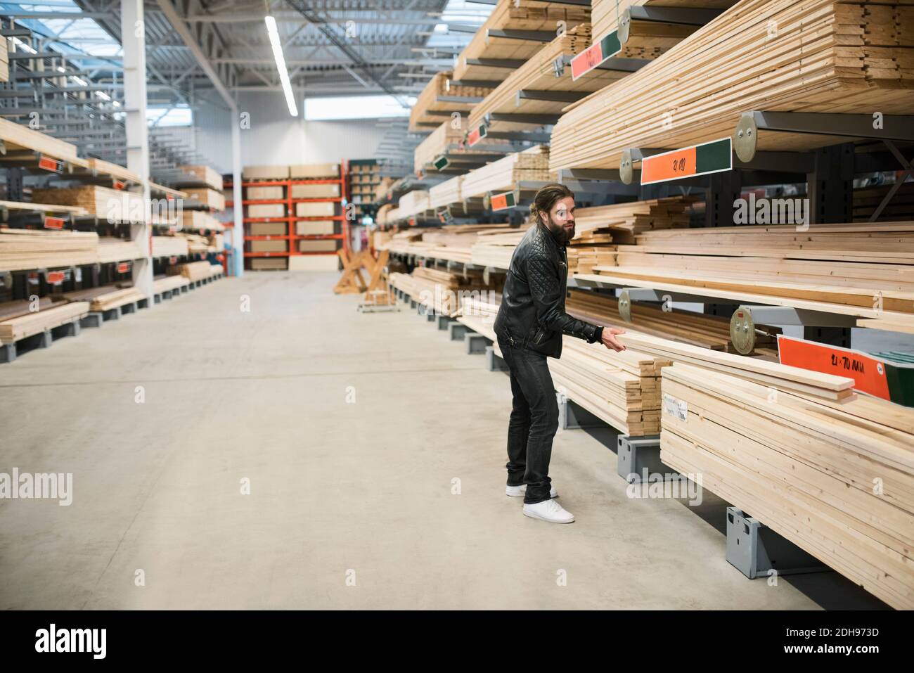 Side view of male customer holding wooden planks by shelves in hardware ...