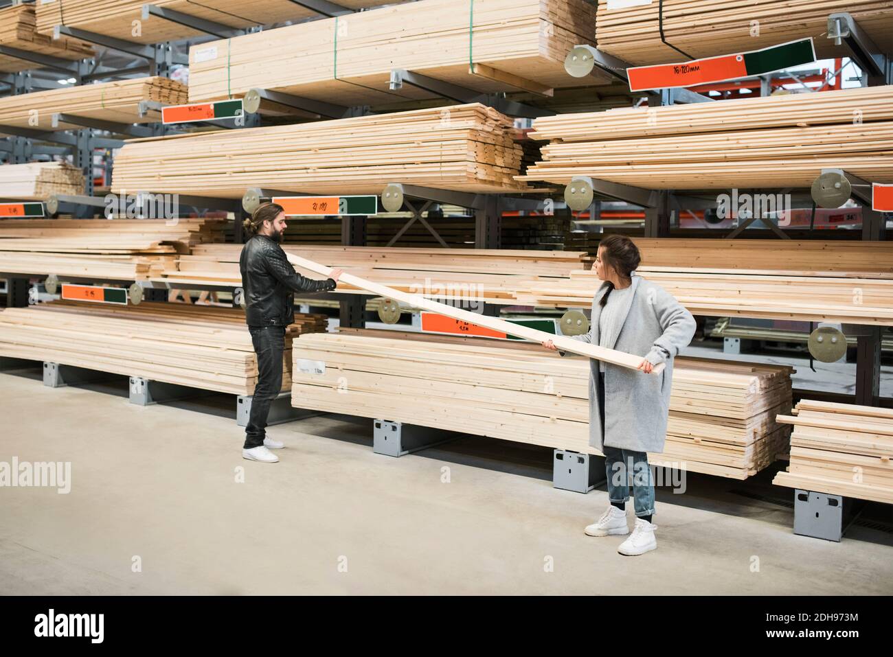 Full length of couple examining wooden plank while standing by shelves ...