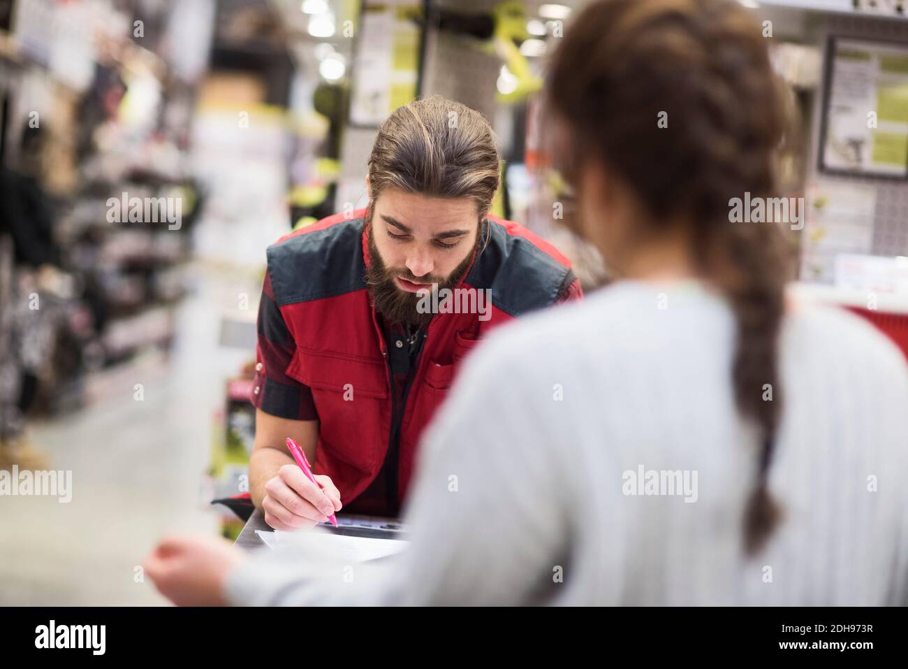 Salesman writing on document while female customer standing in hardware ...