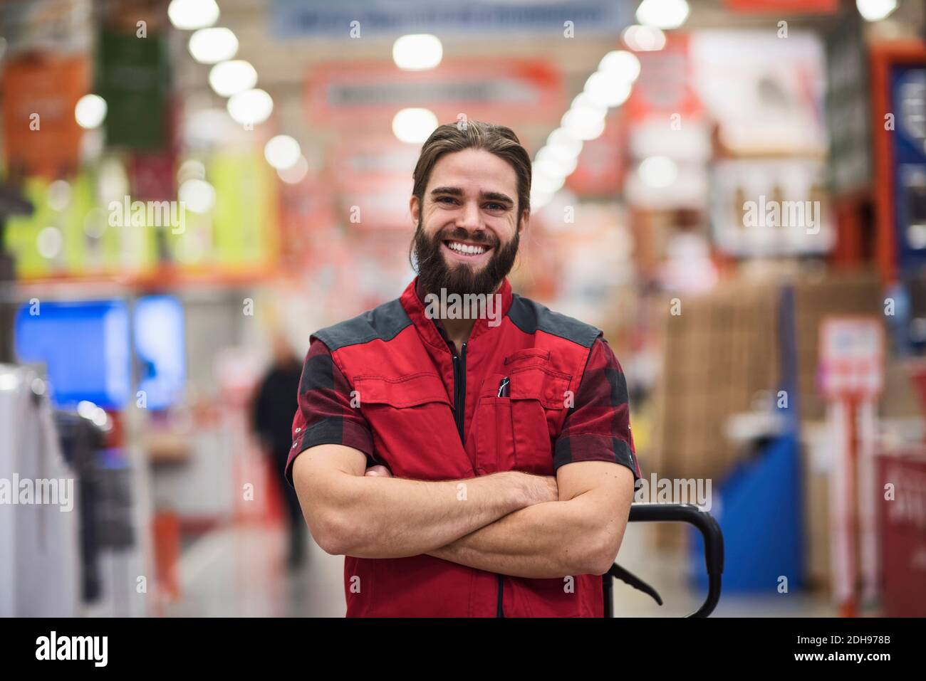 Portrait of happy salesman standing arms crossed at hardware store ...