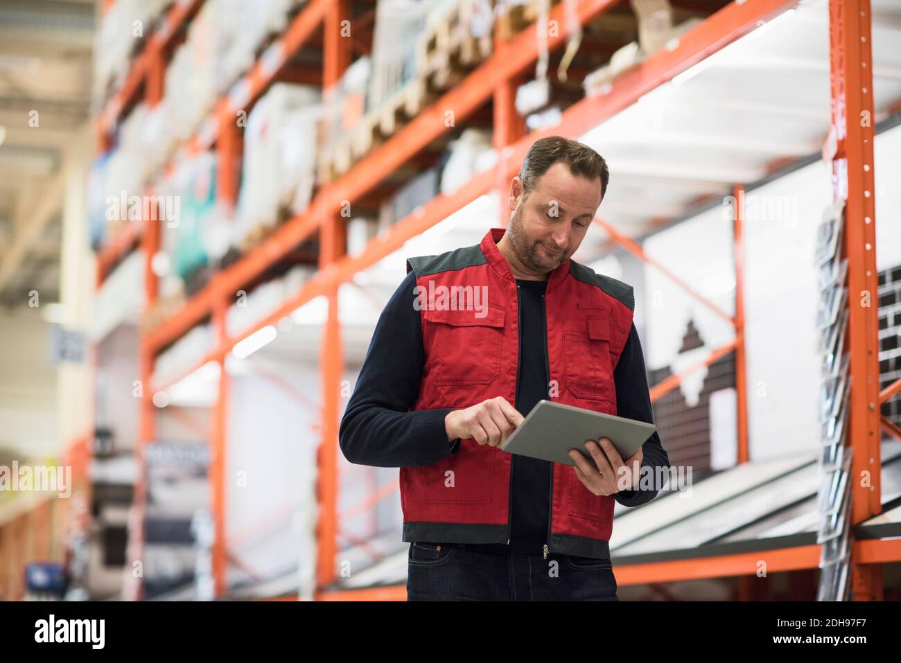 Salesman using digital tablet while standing by shelf in hardware store ...