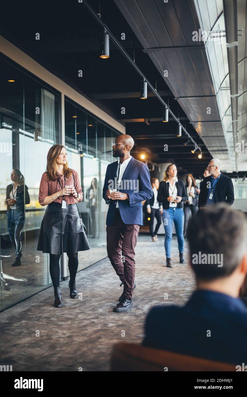 Female and male coworkers walking and talking in corridor at workplace ...