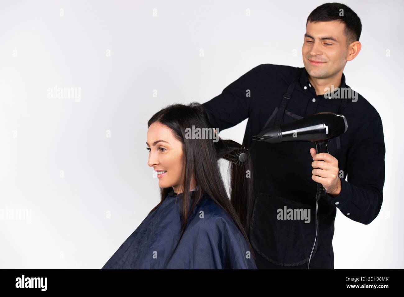 A professional male hairdresser dries a young woman's hair with a foen ...
