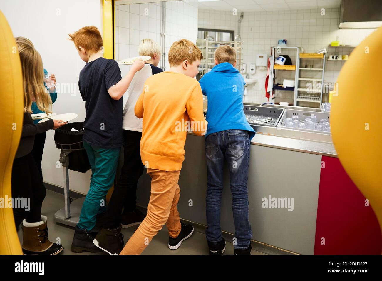 Children putting plates in crate after having lunch at school cafeteria ...