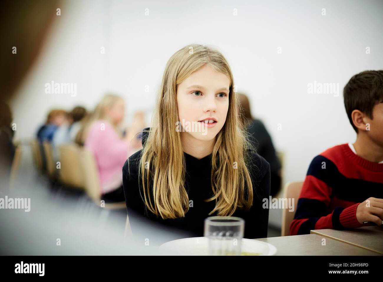 Thoughtful girl sitting at table during lunch break in school cafeteria ...