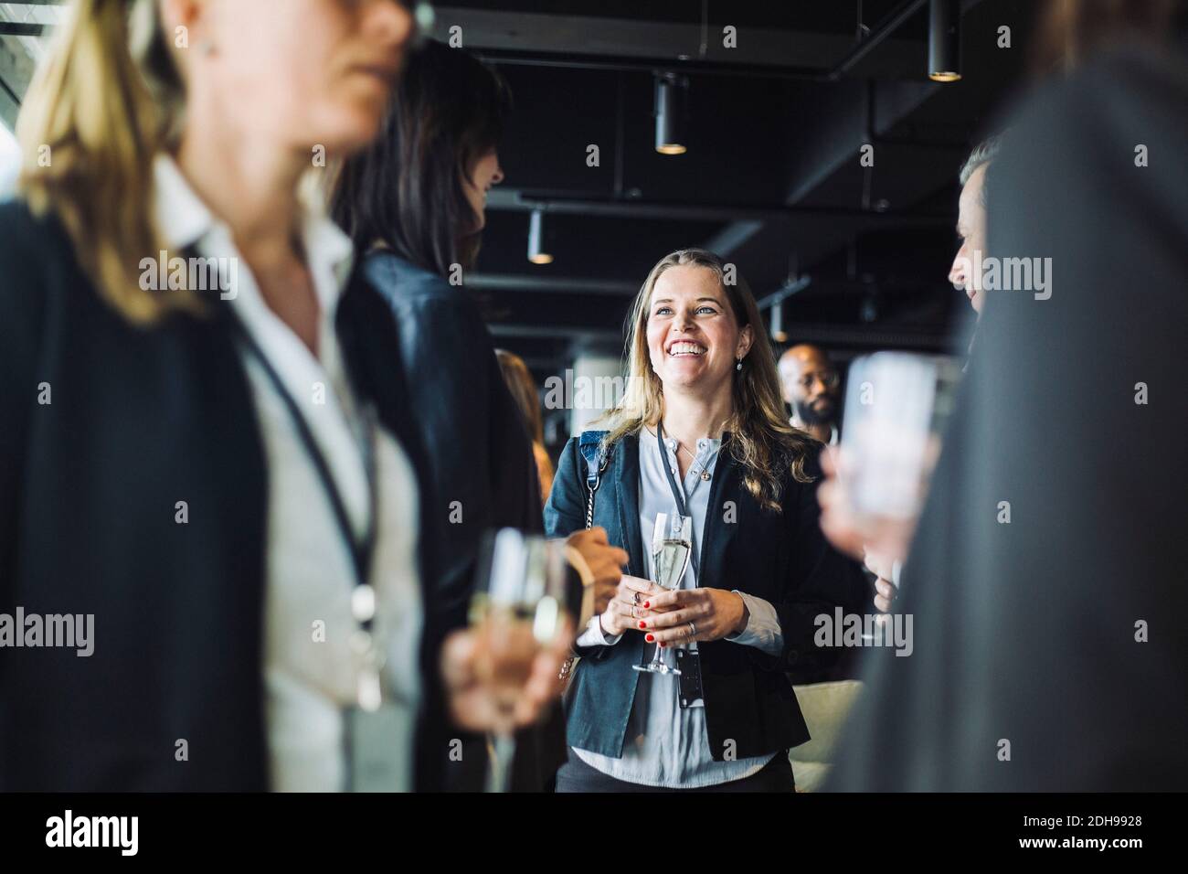 Smiling female business person talking with coworkers while holding ...