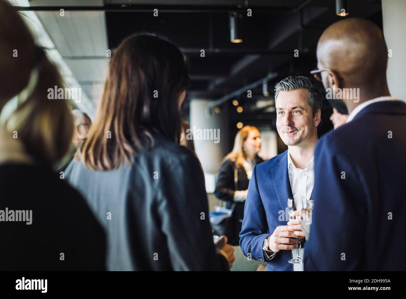 Smiling entrepreneur talking to colleagues while holding drinking glass ...